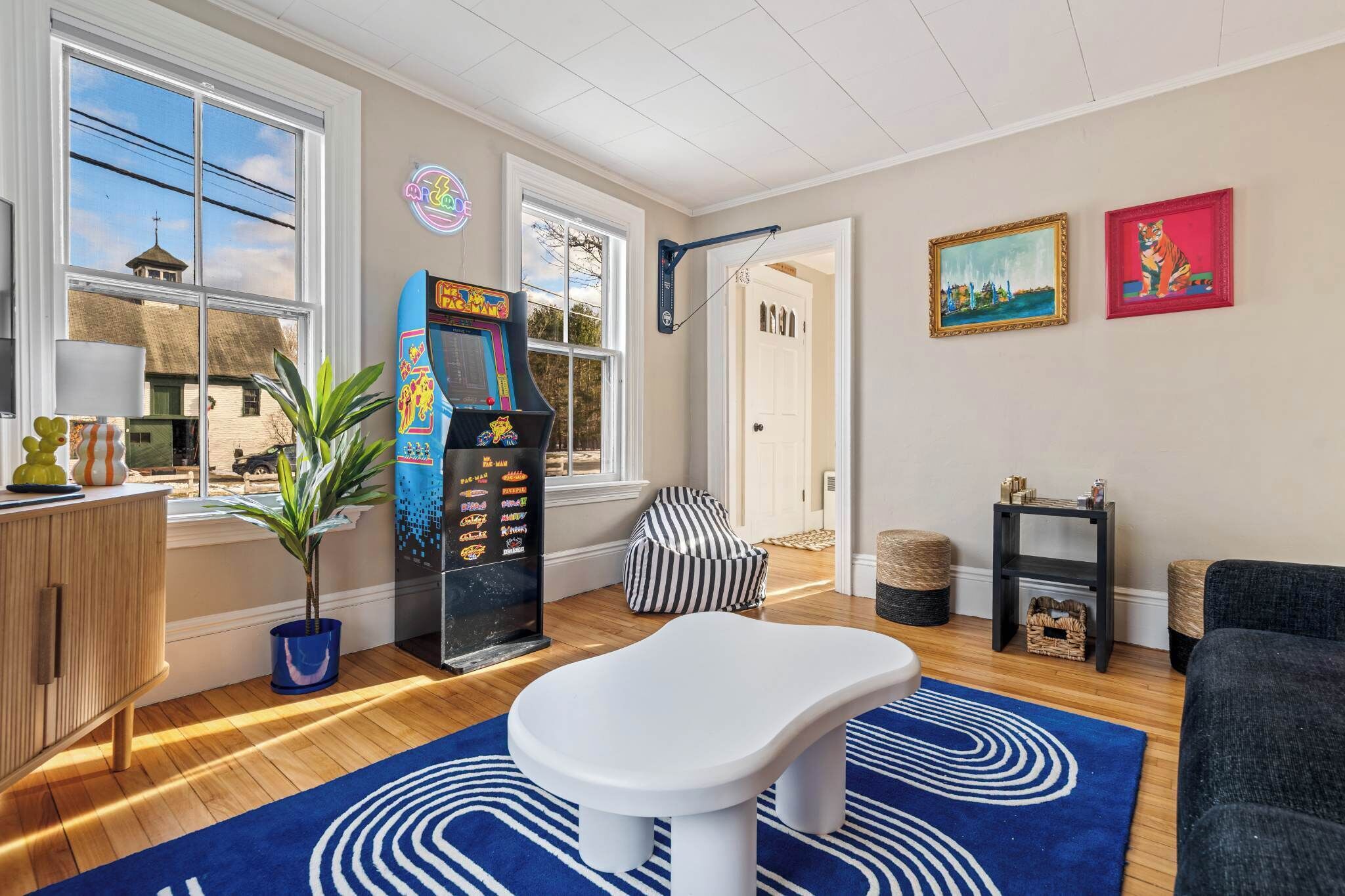Uma sala de estar moderna com uma janela grande, um console de jogos, uma poltrona de grão de espuma e um tapete azul estampado.