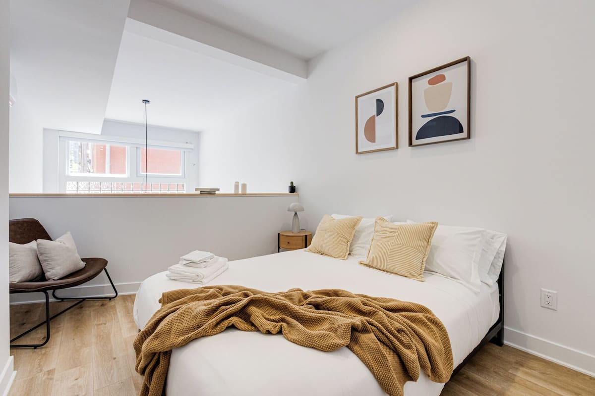 Quarto com cama, cadeira, mesa de cabeceira e janela.