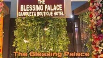 A entrada do The Blessing Palace Banquet & Boutique Hotel, com uma placa e plantas decorativas.
