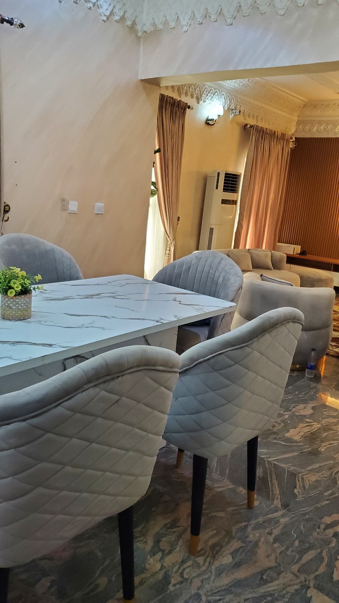 Uma sala de jantar com mesa de mármore, cadeiras estofadas e um ar condicionado moderno.
