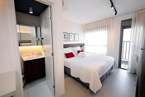 Quarto de hotel com cama, banheiro com espelho e janela com cortinas.