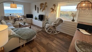 Uma sala de estar aconchegante com sofá, poltrona de balanço, mesa de centro e televisão.