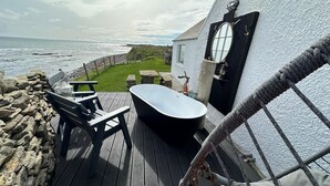 Um terraço com uma banheira preta, parede de pedra e vista para o mar.