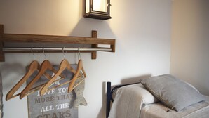 Quarto com uma cama, um cabideiro de madeira com ganchos e um letreiro fixado na parede.