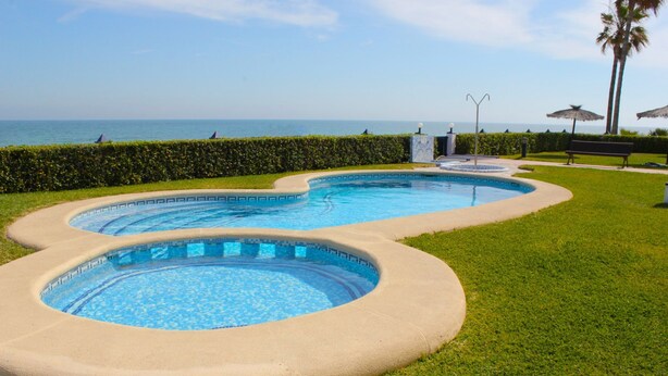 Piscina com design curvo, cercada por gramado bem cuidado e um hedge.
