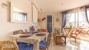 Uma área de refeições com uma mesa de madeira posta para quatro pessoas, cercada por cadeiras de vime com almofadas azuis. Uma mesa de centro de madeira está no centro.