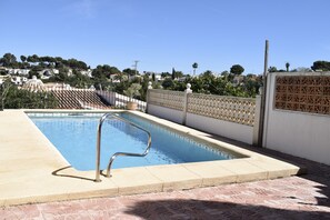 Piscina retangular com escada de metal, cercada por um deck revestido de azulejos e um cercado decorativo.