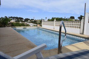 Uma piscina com escada de metal, cerca branca e vista de edifícios ao fundo.