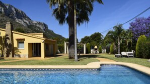 Piscina com montanhas ao fundo, um edifício amarelo e vegetação bem cuidada.