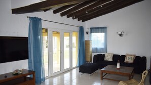 Uma sala de estar com um sofá, uma mesa de centro, uma televisão e uma poltrona de vime.