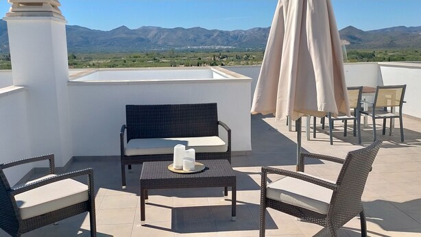 Um terraço com móveis de vime, uma mesa com velas e vista para montanhas.