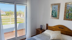 Quarto com uma grande porta de vidro deslizante que dá para uma varanda, uma cama de madeira com colcha estampada e dois quadros florais na parede.