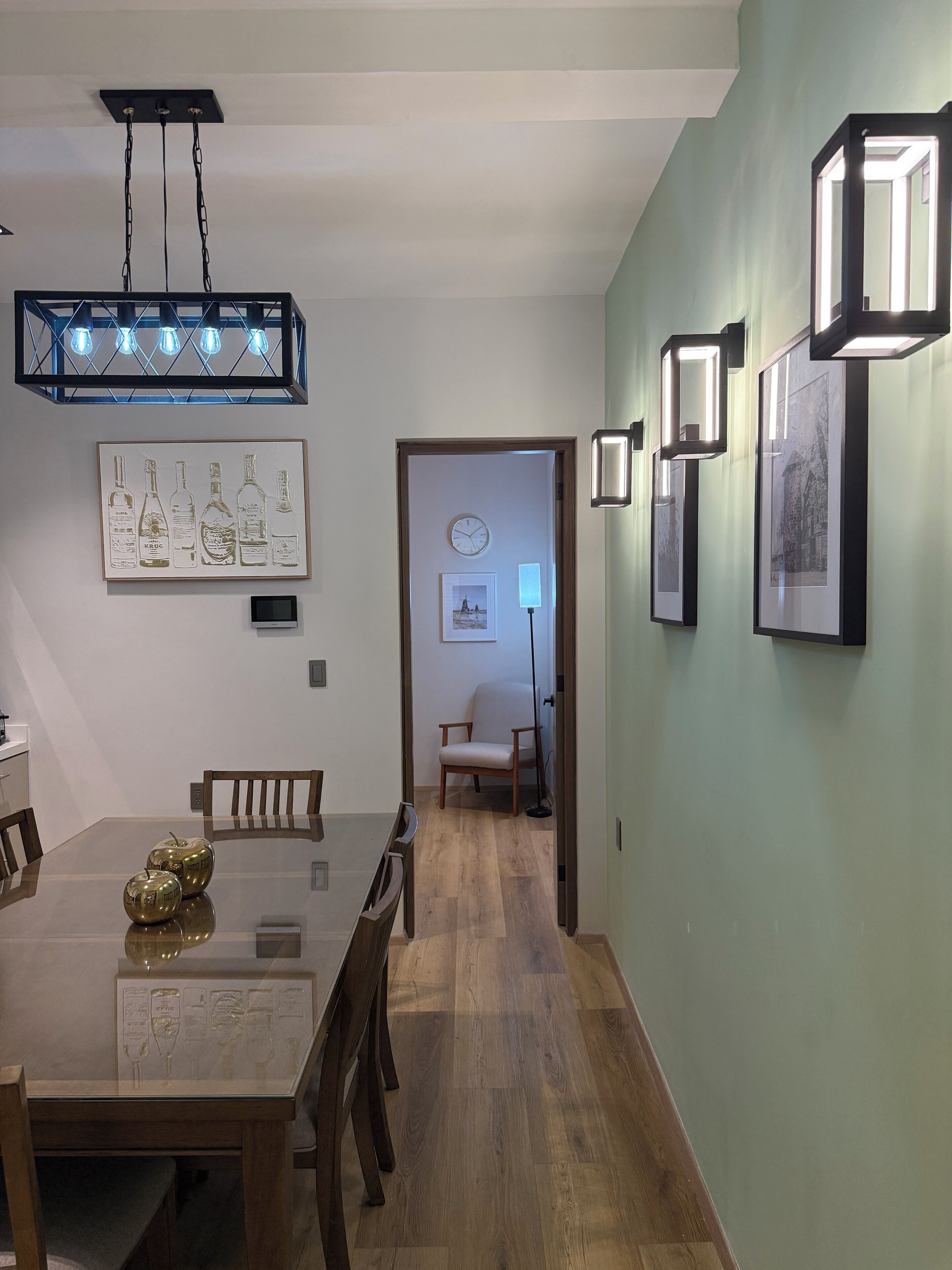 Uma sala de jantar com mesa de madeira, cadeiras e um candelabro. Há quadros nas paredes e um relógio na parede.