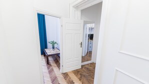 Um corredor com piso de madeira em padrão herringbone, uma porta branca e uma cortina azul.