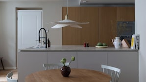 Cozinha moderna com mesa de jantar de madeira, cadeiras brancas, luminária pendente branca e armário branco.