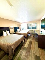 Quarto de hotel com duas camas, uma mesa de trabalho e uma janela grande com persianas.