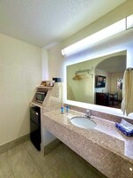 Casa de banho com bancada de granito, lavatório, espelho, porta-toalhas e micro-ondas.
