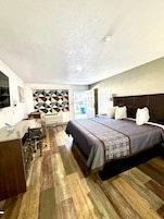 Quarto de hotel com uma cama grande, uma escrivaninha com cadeiras e um papel de parede estampado.