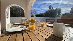 Mesa de madeira posta para o café da manhã, com pratos, copos e uma jarra de suco de laranja.
