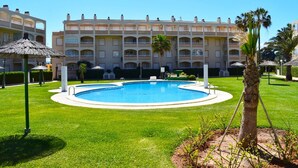 Uma piscina cercada por um gramado bem cuidado, com um edifício de vários andares ao fundo.
