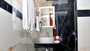 Um banheiro moderno com piso de mármore, área de chuveiro com azulejos preto e branco, vaso sanitário branco e pia com espelho acima.