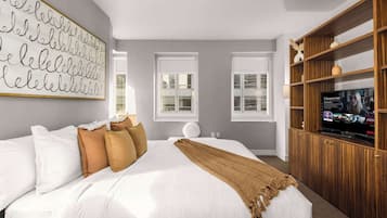 Quarto com uma cama grande, um suporte de TV de madeira e uma parede com um letreiro decorativo.
