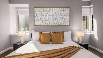 Quarto moderno com uma cama grande, duas mesas de cabeceira com abajures, um detalhe decorativo na parede e janelas amplas.