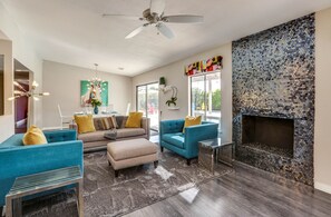 Uma sala de estar moderna com lareira, sofás e ventilador de teto.