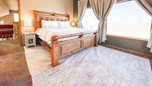 Um quarto com cama de madeira, mesa de cabeceira, luminária, espelho e janela com cortinas.
