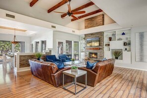 Uma sala de estar espaçosa com lareira de pedra, sofás de couro e ventilador de teto.