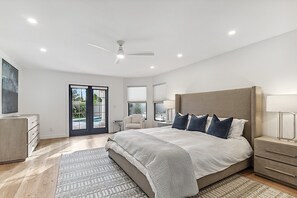 Quarto moderno com uma cama grande, um ventilador de teto e vista através das portas de vidro.