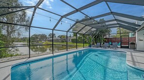 Piscina com cobertura de vidro, espreguiçadeiras e vista para um lago e casas.