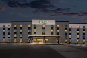 Um edifício moderno de hotel com telhado plano, várias janelas e uma placa indicando 'Woodspring Suites'.