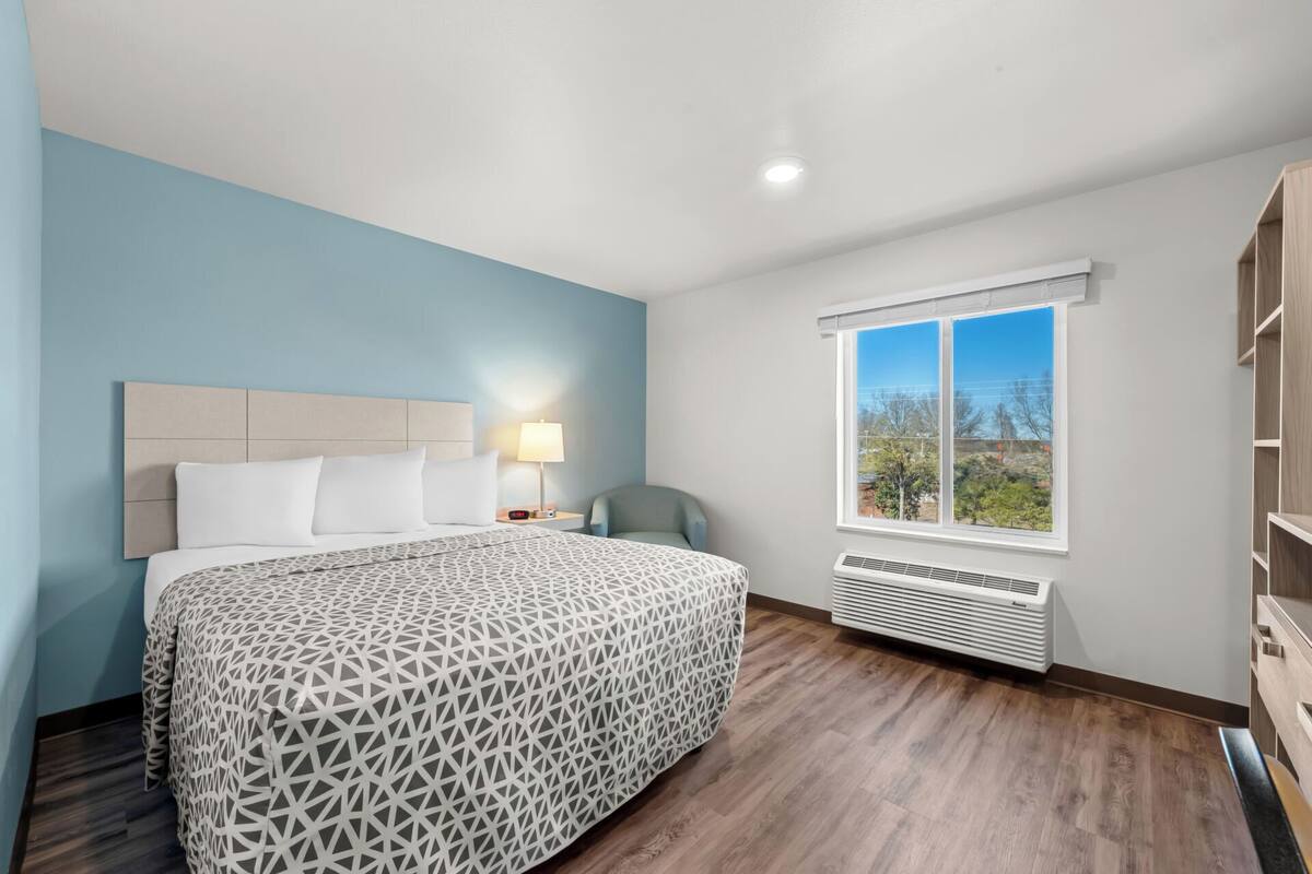 Quarto de hotel com cama, mesa de cabeceira, luminária, cadeira, janela com vista e aquecedor embutido.