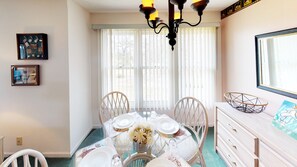 Uma sala de jantar com mesa de vidro, cadeiras brancas, um candelabro e um aparador com espelho.