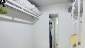 Um roupeiro pequeno e fechado com estantes brancas, um espelho e soalho de madeira.
