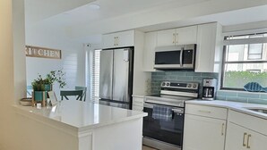 Uma cozinha moderna com armários brancos, geladeira de aço inoxidável, micro-ondas, forno e cafeteira.