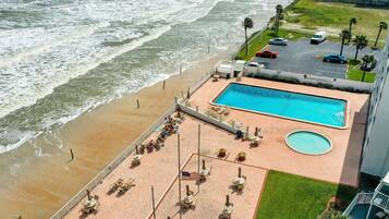 Vista aérea de um hotel na praia com piscina, área de estar à beira-mar e estacionamento.