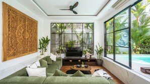Sala de estar moderna com um sofá verde, uma televisão e uma grande janela com vista para uma piscina.
