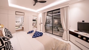 Quarto de hotel moderno com uma cama grande, um ventilador de teto, uma televisão e uma porta de vidro deslizante para uma varanda.