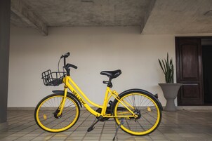 Uma bicicleta amarela com cesto, estacionada em um piso de azulejos, em ambiente interno.