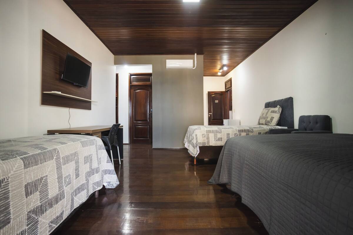 Quarto de hotel com duas camas, uma televisão presa na parede e teto de madeira.