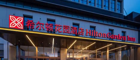 Exterior do Hilton Garden Inn, com fachada moderna, grande entrada de vidro e sinalização destacada.