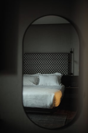 Uma cama com roupa de cama branca e uma cabeceira estampada, vista através de um moldura de janela circular.