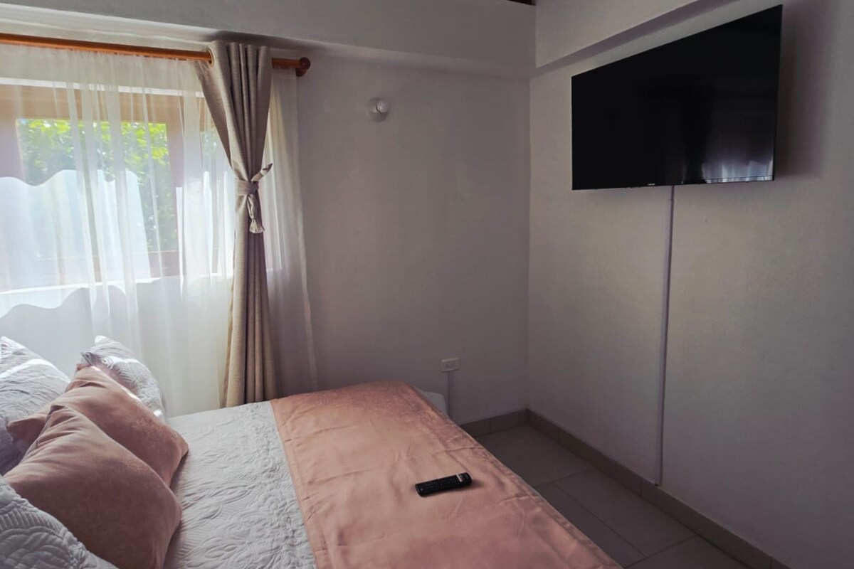 Quarto com cama, televisão na parede e janela com cortinas.