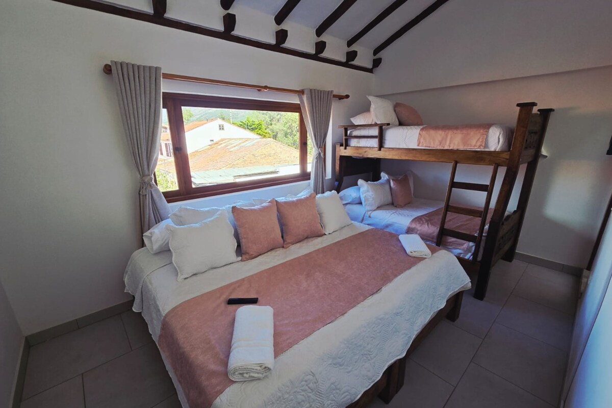 Quarto com beliche, janela, cortinas e cama com travesseiros e cobertor.