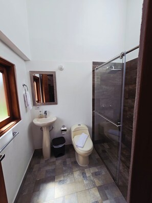 Casa de banho compacta com lavatório pedestal, sanita e cabine de duche com vidro.