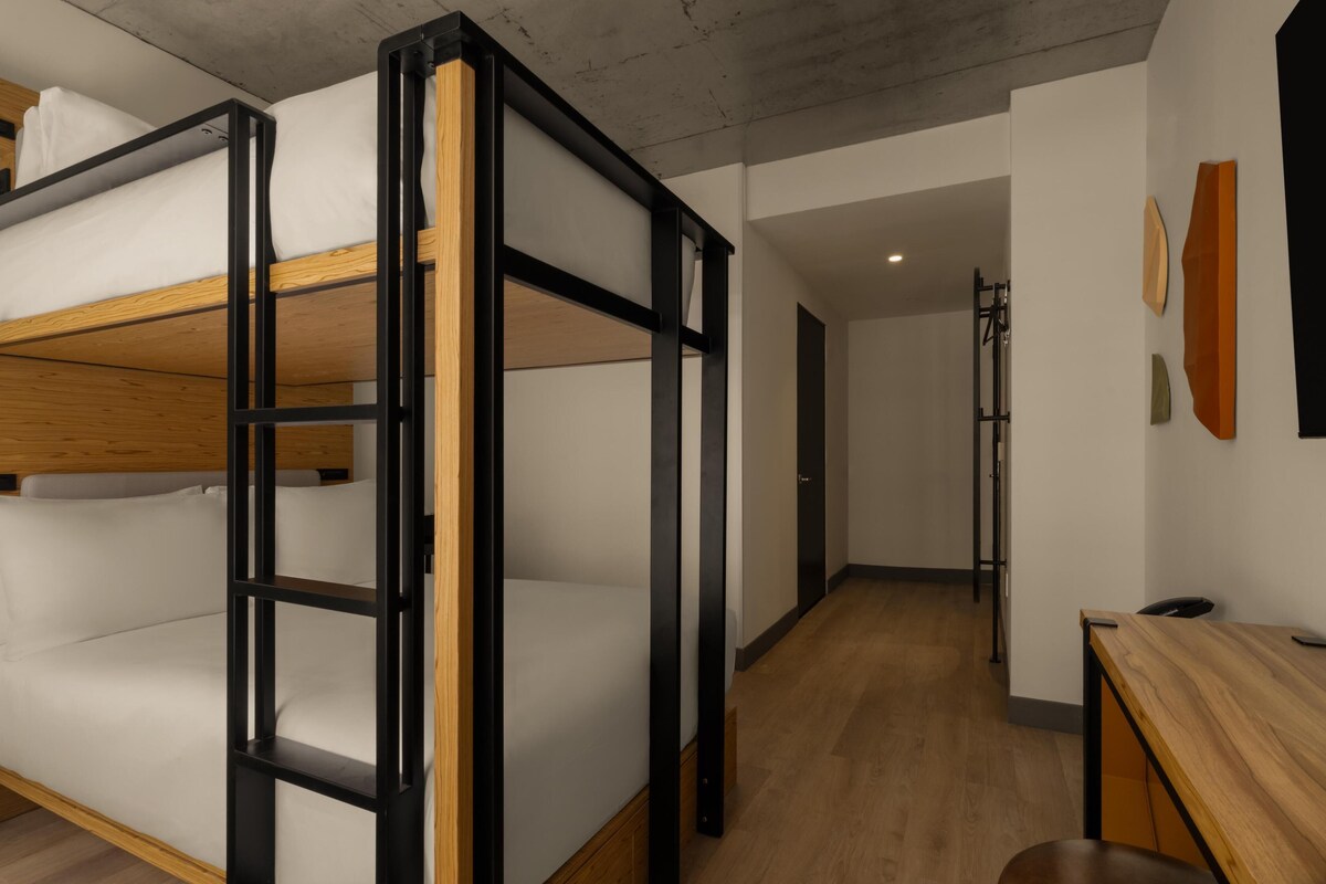 Quarto moderno com beliches, uma escrivaninha de madeira e uma porta que dá para outro quarto.