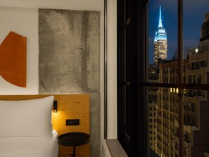 Quarto de hotel com cama, uma mesinha redonda, um painel de parede em madeira e vista para o Empire State Building.
