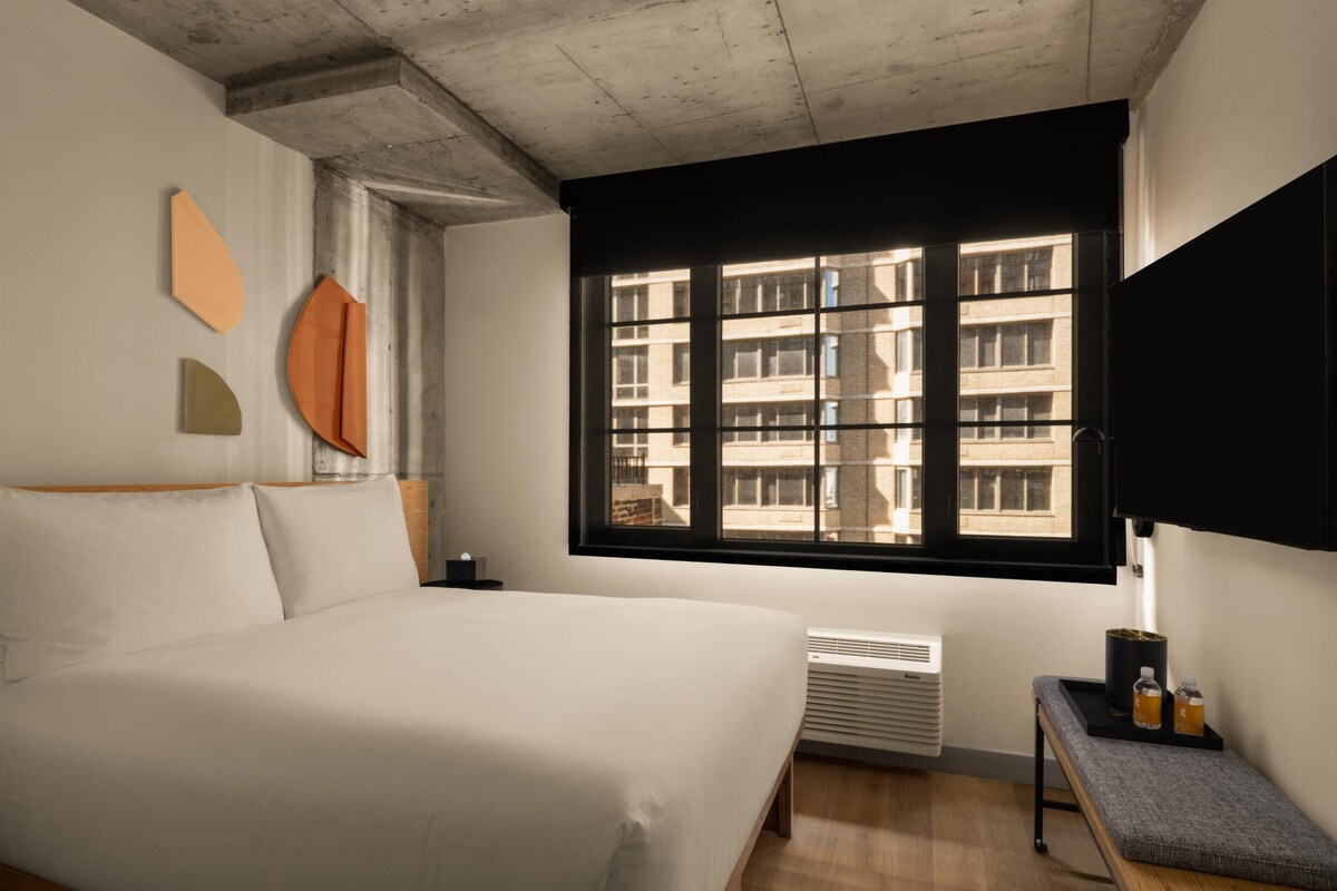 Quarto com cama, janela, radiador e uma pequena mesa com garrafas.